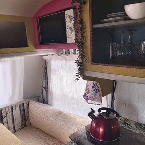Cozinha compacta com micro-ondas, chaleira e um armário com louças.