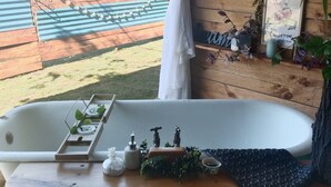 Casa de banho com banheira, prateleira de madeira com plantas e vista para um deck de madeira e colinas.