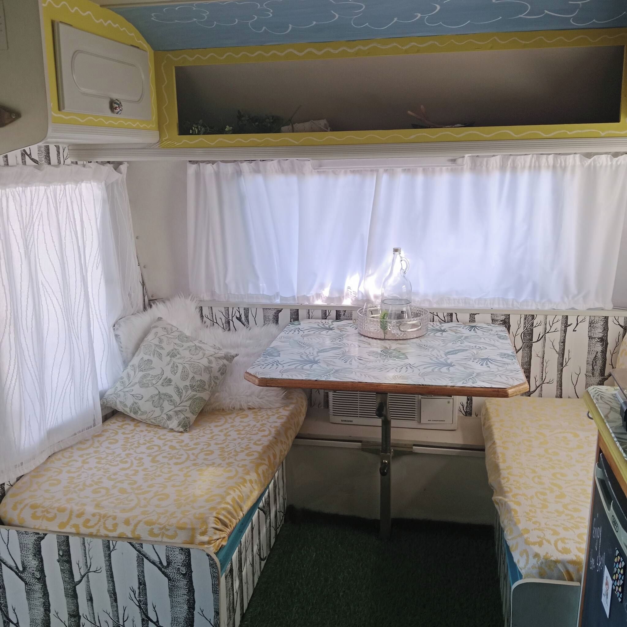 Interior acolhedor de uma RV, com mesa de jantar, assentos estofados e janela com cortinas.