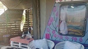 Uma área de estar acolhedora ao ar livre, com mesa e cadeiras, um vaso decorativo e uma van camper com detalhes florais.
