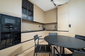 Cozinha compacta com micro-ondas embutido, fogão e área de refeições com mesa redonda e cadeiras.