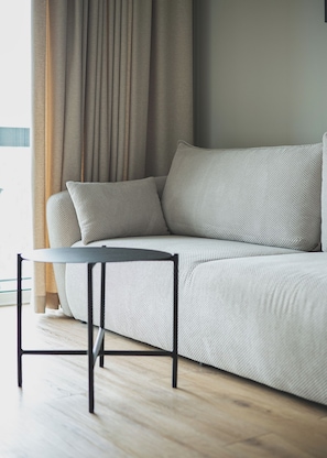 Uma sala de estar moderna com um sofá cinzento, uma pequena mesa preta e piso de madeira.