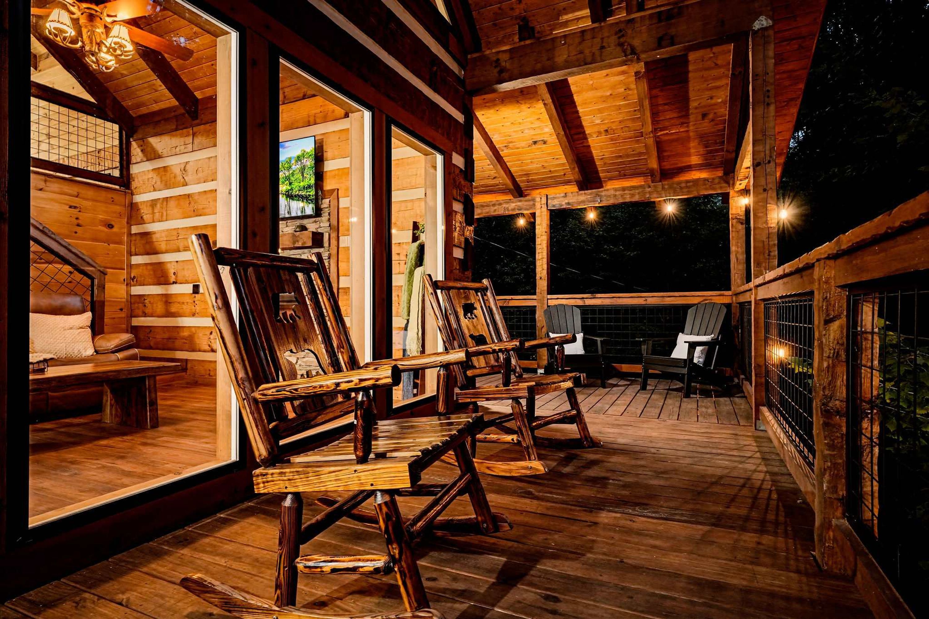 Interior de cabana de madeira com varanda, cadeiras rústicas de madeira e lareira de pedra.