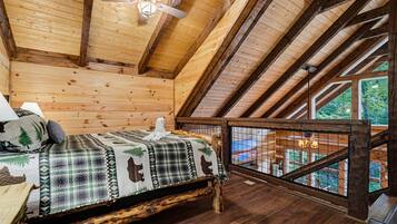 Quarto de cabana aconchegante com teto de madeira, cama com colcha xadrez e vista para um deck de madeira lá fora.