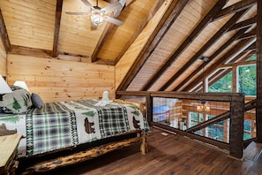 Quarto de cabana aconchegante com teto de madeira, cama com colcha xadrez e vista para um deck de madeira lá fora.