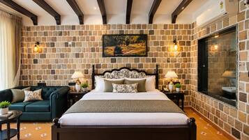 Quarto com parede de pedra, cama com cabeceira, duas mesas de cabeceira com abajures, um sofá verde e uma janela.