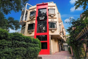 Edifício de hotel com uma característica vermelha vertical marcante, várias janelas e entrada com portão.