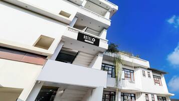 Um hotel com vários andares, um letreiro chamativo com a palavra 'HOTEL', uma escadaria e uma varanda com plantas.