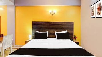 Quarto de hotel com uma cama grande, mesa de cabeceira com abajur, uma cadeira e luminária na parede.