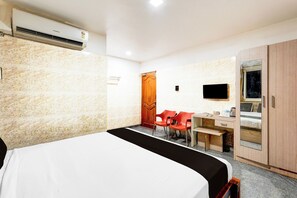 Quarto de hotel com cama, escrivaninha, cadeira, televisão e armário.
