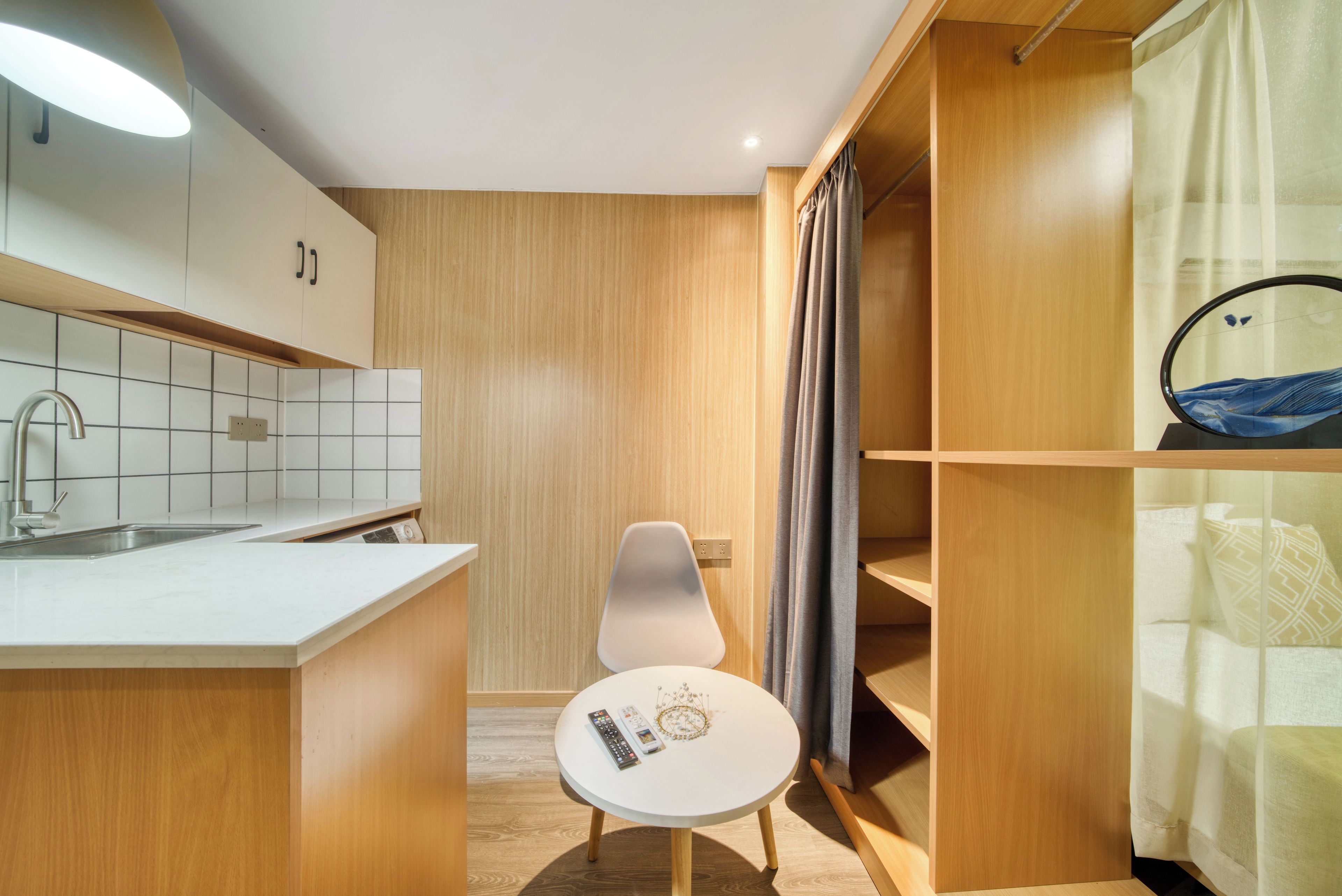 Quarto de hotel compacto com cozinha compacta, uma pequena mesa redonda e um controle remoto, e uma cama com edredom branco.