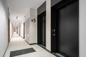 Um corredor com piso demarcado por um padrão de azulejos pretos e brancos, parede com design listrado vertical e uma porta com o símbolo de número.
