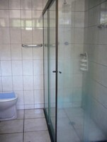 Box de chuveiro com paredes de vidro e vaso sanitário à esquerda.