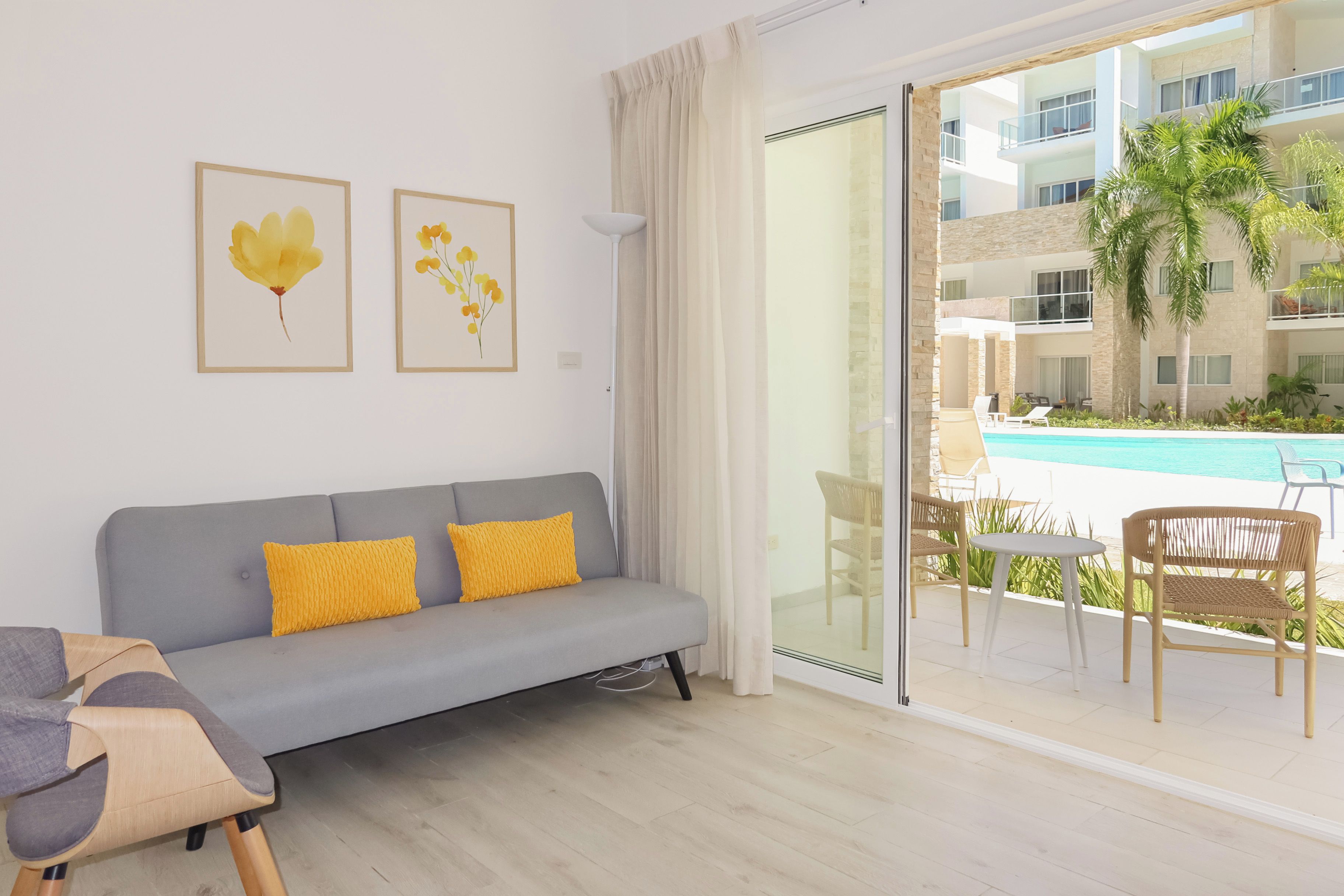 Sala de estar moderna com um sofá cinza, dois almofadas amarelas e uma porta de vidro que dá para uma varanda com vista para a piscina.