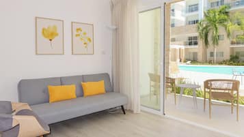 Sala de estar moderna com um sofá cinza, dois almofadas amarelas e uma porta de vidro que dá para uma varanda com vista para a piscina.
