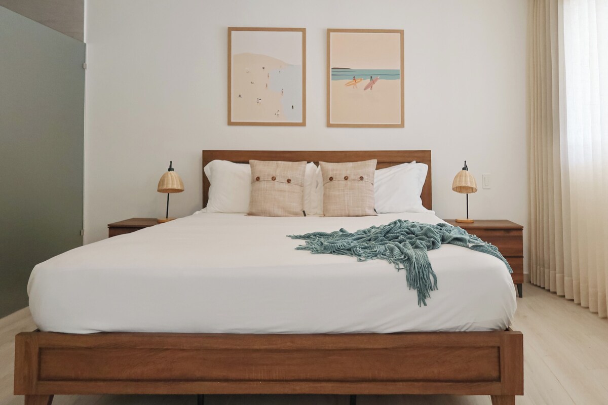 Quarto com cama de madeira, duas mesas de cabeceira e duas luminárias fixadas na parede.