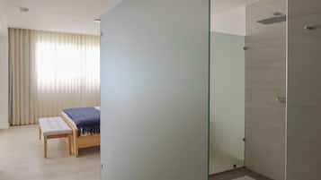 Quarto moderno com cama, um banquinho, divisória de vidro e área de chuveiro.