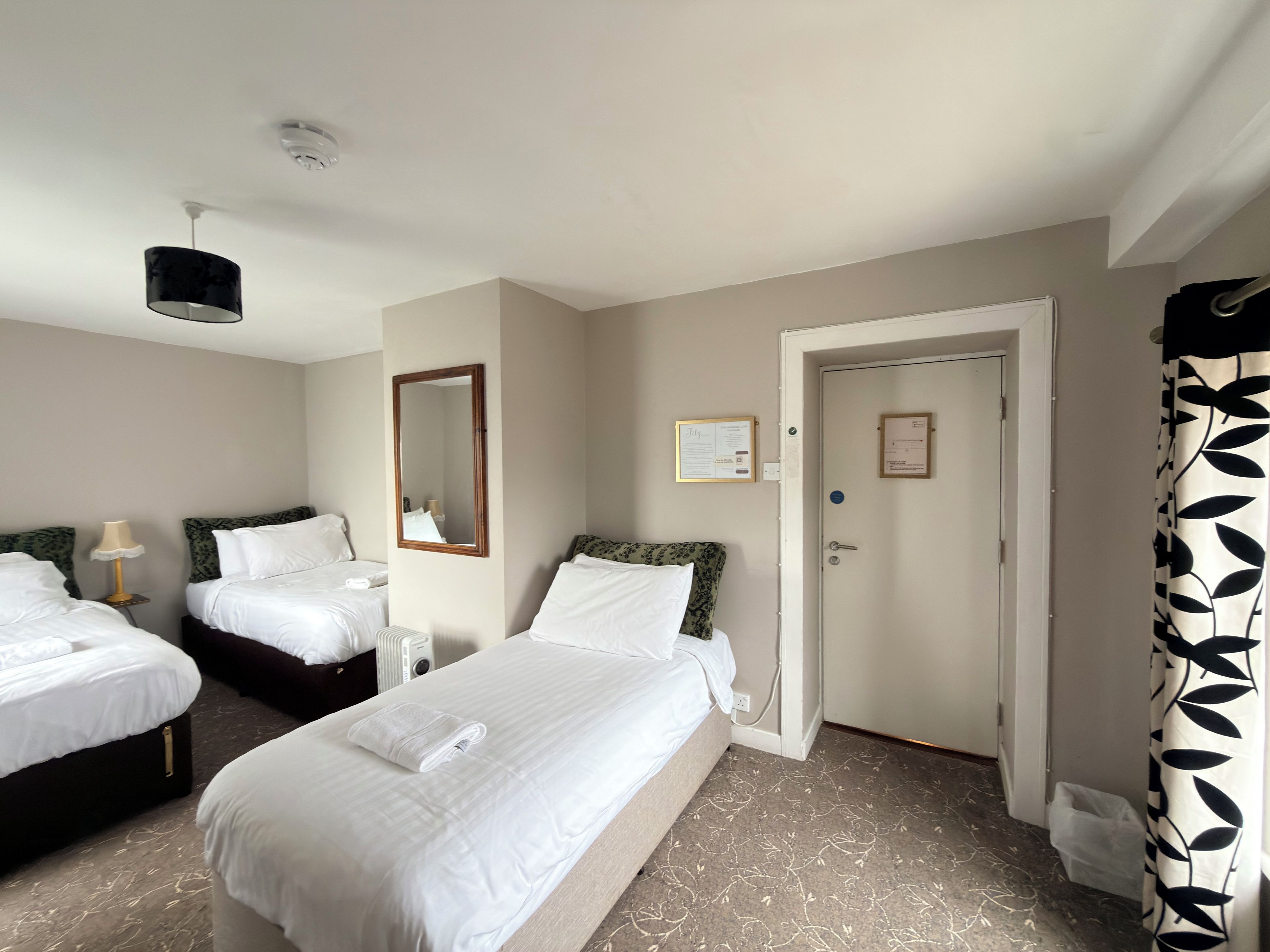 Quarto de hotel com duas camas, um espelho, uma porta com uma placa e um tapete estampado.