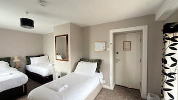 Quarto de hotel com duas camas, um espelho, uma porta com uma placa e um tapete estampado.