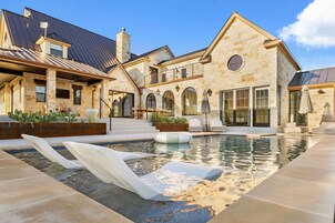 Uma casa luxuosa com piscina, fachada de pedra e várias janelas.