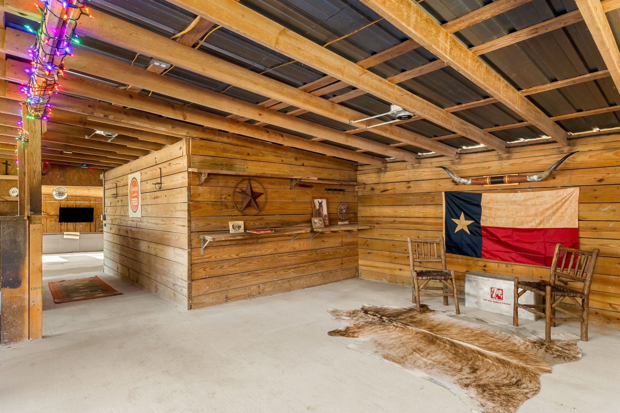 Interior rústico com paredes de madeira, uma bandeira do Texas, uma roda de ferradura e um tapete de couro de vaca.