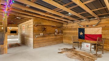Interior rústico com paredes de madeira, uma bandeira do Texas, uma roda de ferradura e um tapete de couro de vaca.