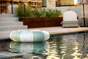 Piscina com um flutuador, escadas para uma área de estar e plantas em vasos.