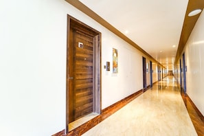 Corredor longo e bem iluminado, com portas de madeira e chão de mármore.