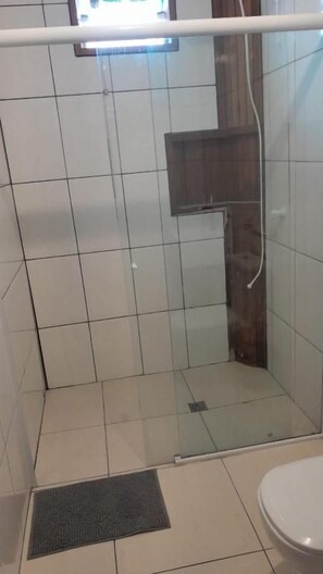 Área de chuveiro com paredes de vidro, piso ladrilhado e um pequeno prateleira.