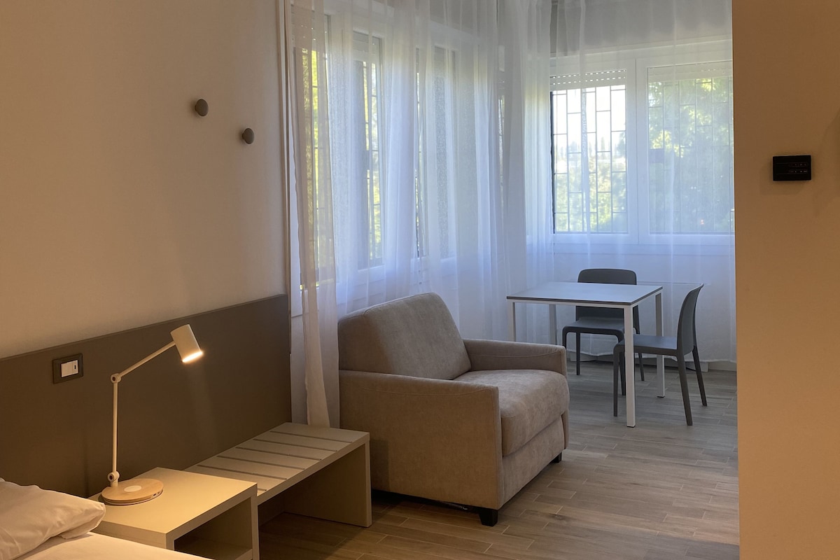 Quarto de hotel com cama, sofá, escrivaninha e mesa de jantar com cadeiras.
