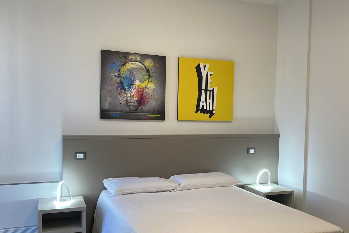 Um quarto moderno com uma cama, mesas de cabeceira e duas obras de arte penduradas na parede.