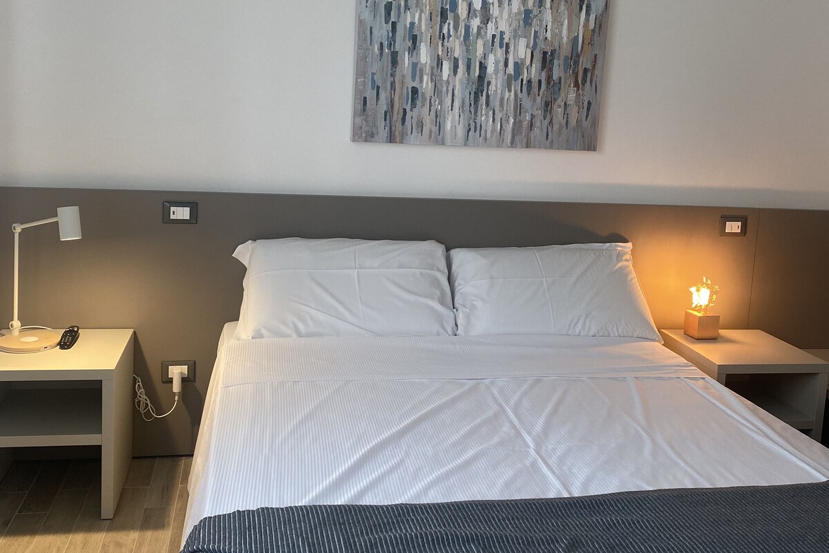 Cama bem arrumada com lençóis brancos, manta listrada cinza e pintura abstrata moderna acima.