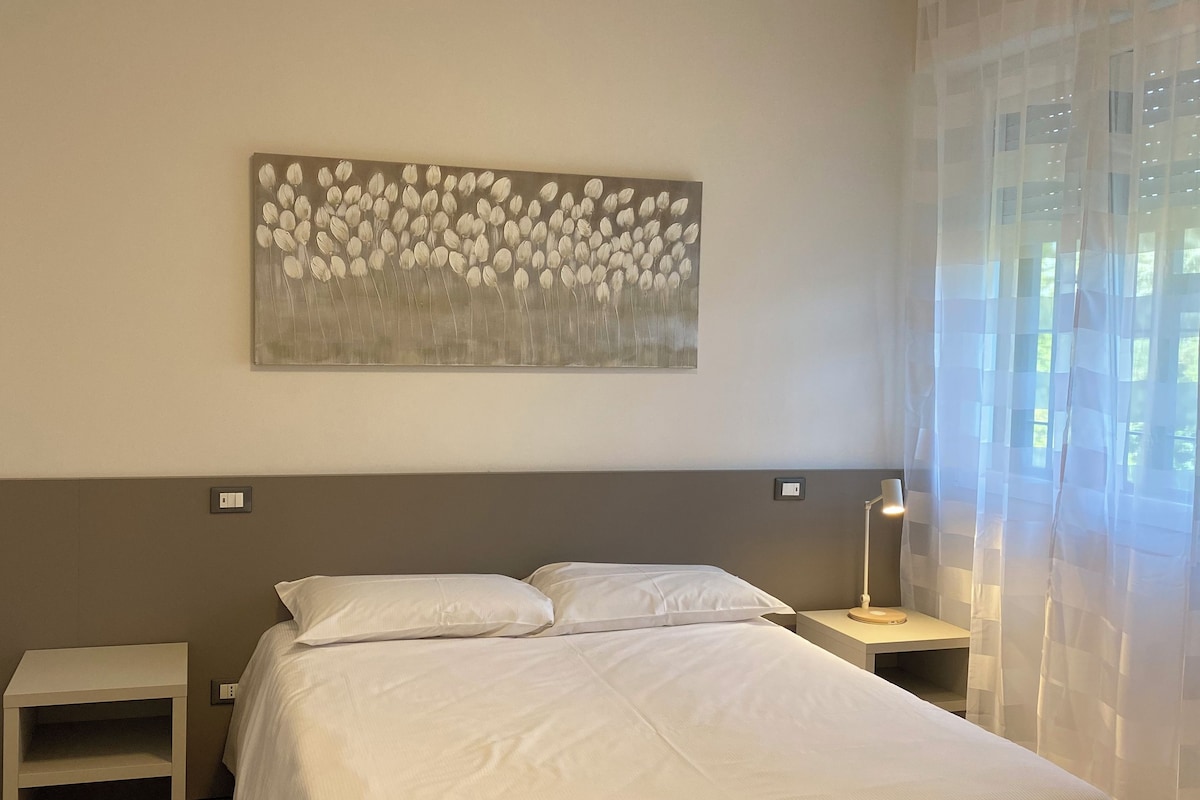 Quarto moderno com cama grande, mesa de cabeceira com abajur e quadro pendurado na parede.