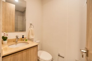 Uma casa de banho com toucador de madeira, sanita branca, espelho e toalha pendurada num suporte de metal.