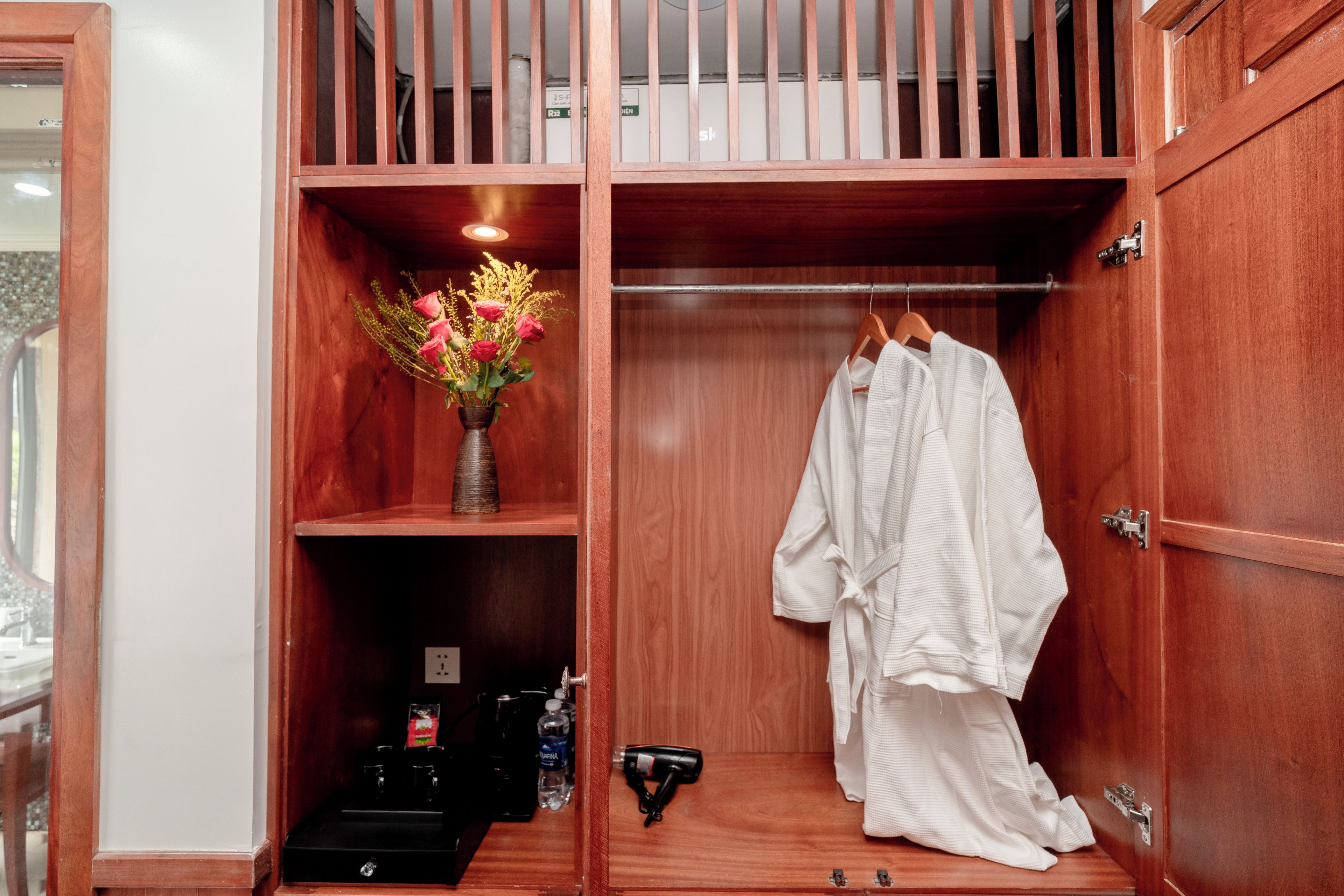 Guarda-roupa de madeira com cabides e um vaso de flores na prateleira superior.