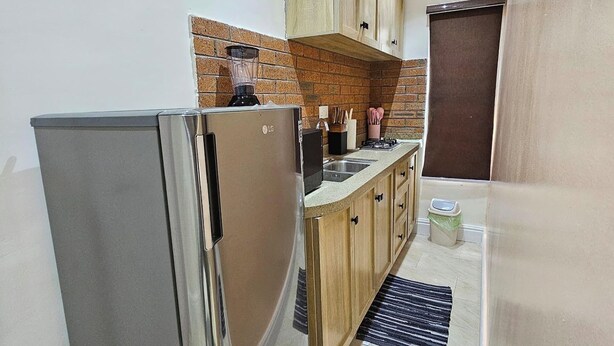 Cozinha compacta com geladeira, armários de madeira, painel de backsplash de tijolos e bancada pequena.