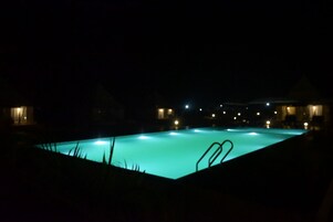 Piscina retangular à noite com iluminação ao redor.