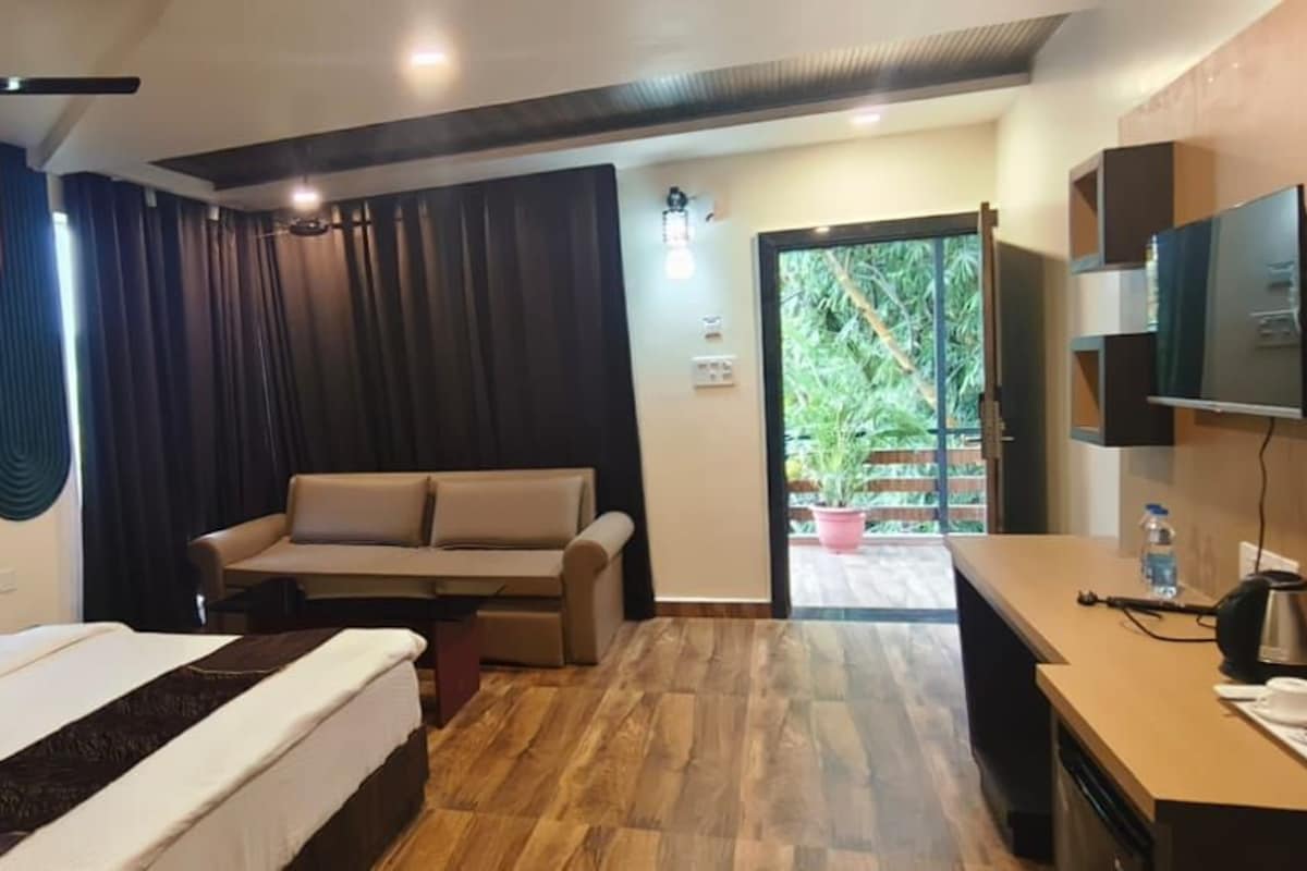 Quarto de hotel com cama, sofá, escrivaninha e televisão, e vista para o exterior.