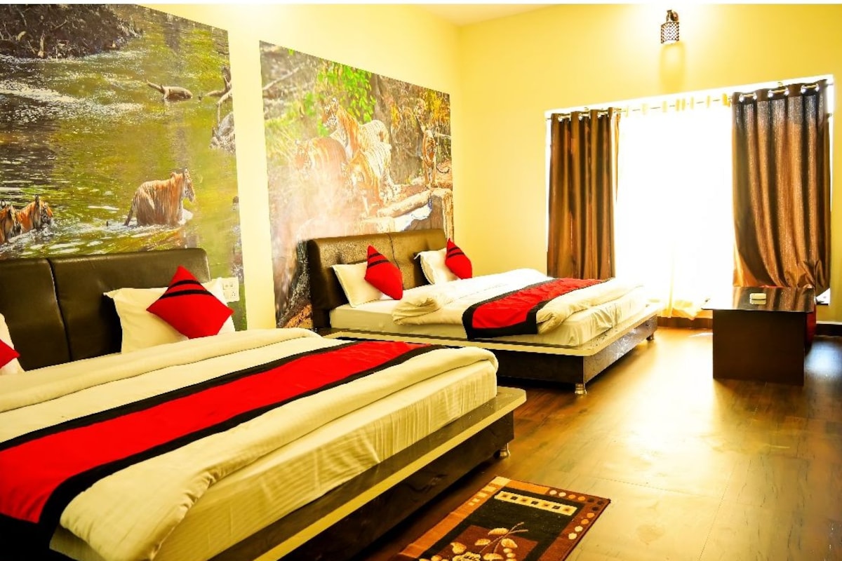 Quarto de hotel com duas camas, cada uma com roupa de cama vermelha e branca, uma pintura grande de uma paisagem fluvial e uma janela com cortinas.