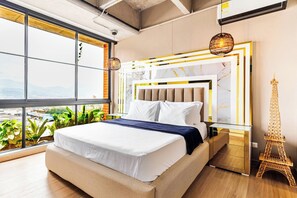 Quarto moderno com uma cama grande, mesa de cabeceira, decoração da Torre Eiffel e vista através de janelas amplas.