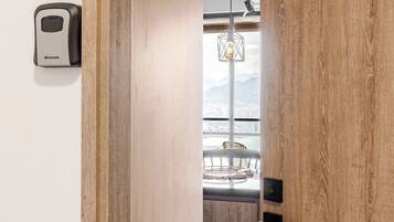 Uma porta de madeira dá acesso a uma varanda com um candeeiro suspenso e vista para a paisagem urbana.