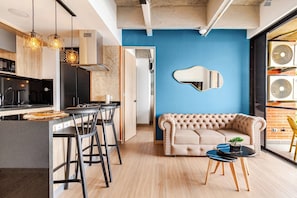 Uma cozinha moderna com área de bar, parede azul de destaque e sofá estofado em um espaço de estar.