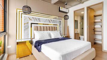 Quarto moderno com cama grande, mesa de cabeceira, guarda-roupa e banheiro visível por uma porta aberta.