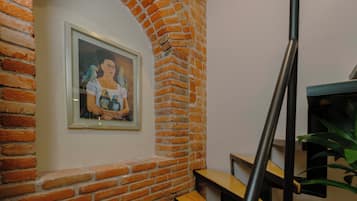 Uma obra de arte emoldurada numa parede de tijolos, um banco de madeira e uma escadaria com guarda-corpo de metal.