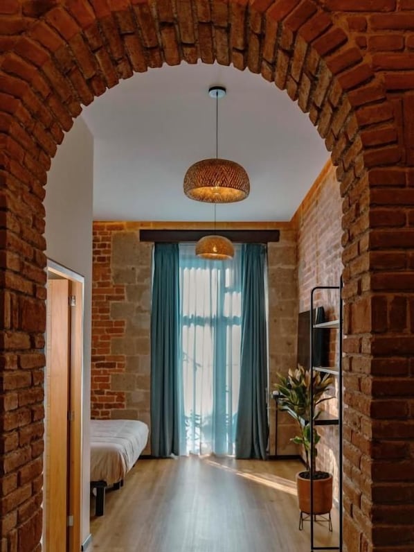 Um corredor estreito com um arco de tijolos, uma cama, um lustre e um vaso de planta.