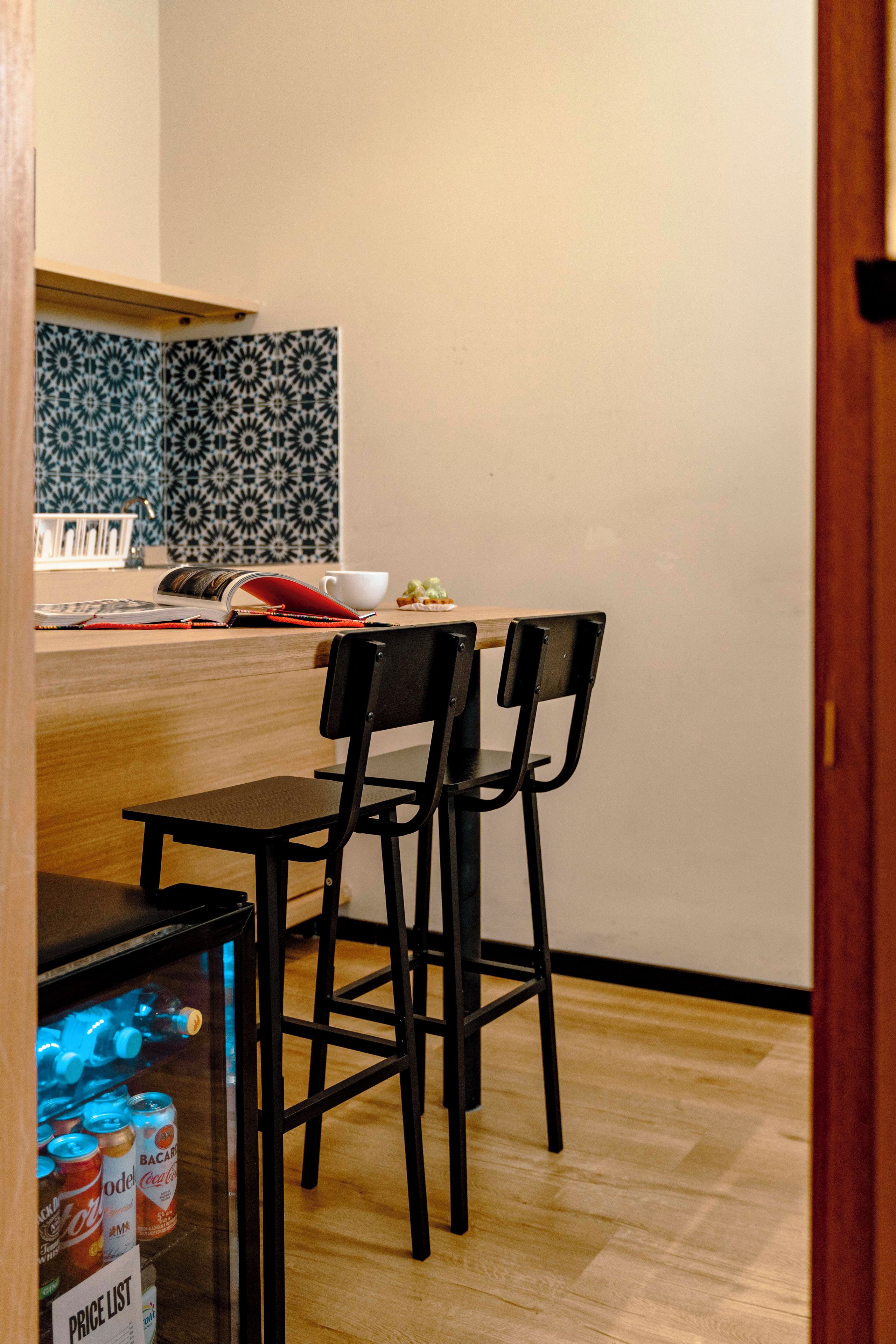 Uma pequena cozinha compacta com uma mesa de madeira, duas cadeiras pretas e um refrigerador cheio de bebidas.