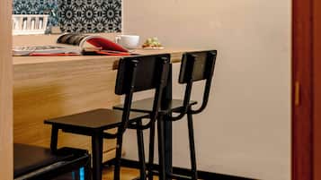 Uma pequena cozinha compacta com uma mesa de madeira, duas cadeiras pretas e um refrigerador cheio de bebidas.