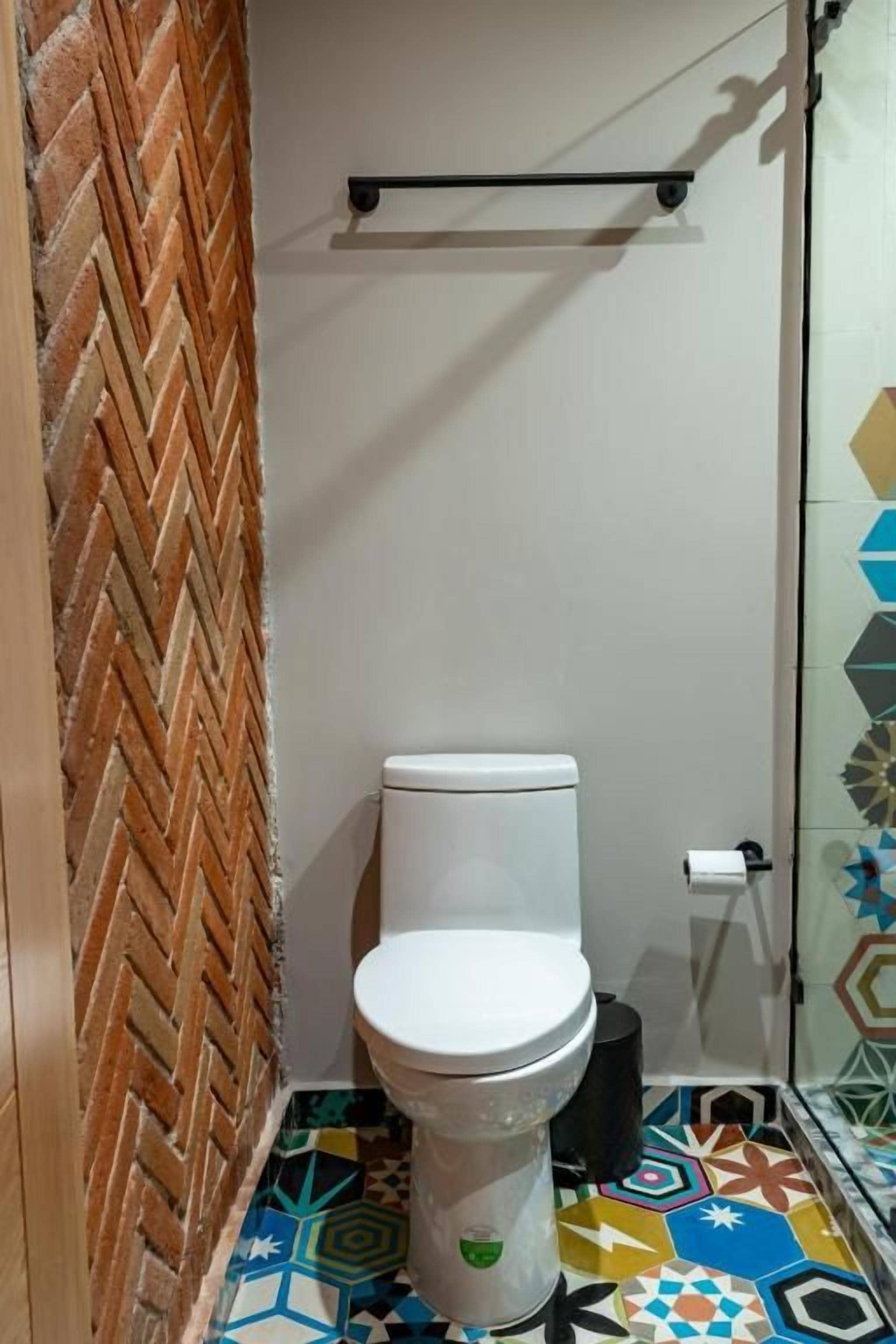 Um banheiro com vaso sanitário branco, lixeira preta e área de chuveiro com porta de vidro.