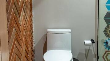 Um banheiro com vaso sanitário branco, lixeira preta e área de chuveiro com porta de vidro.