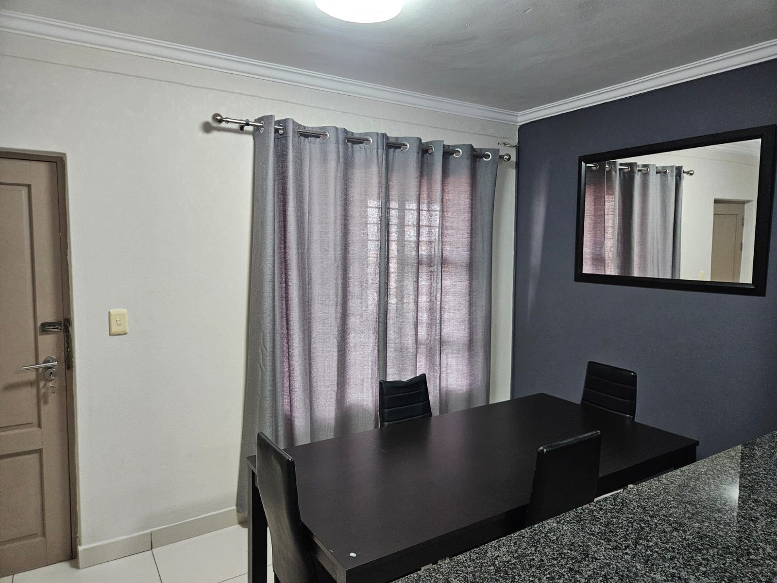 Quarto com uma mesa de jantar, cadeiras, uma porta e um espelho na parede.